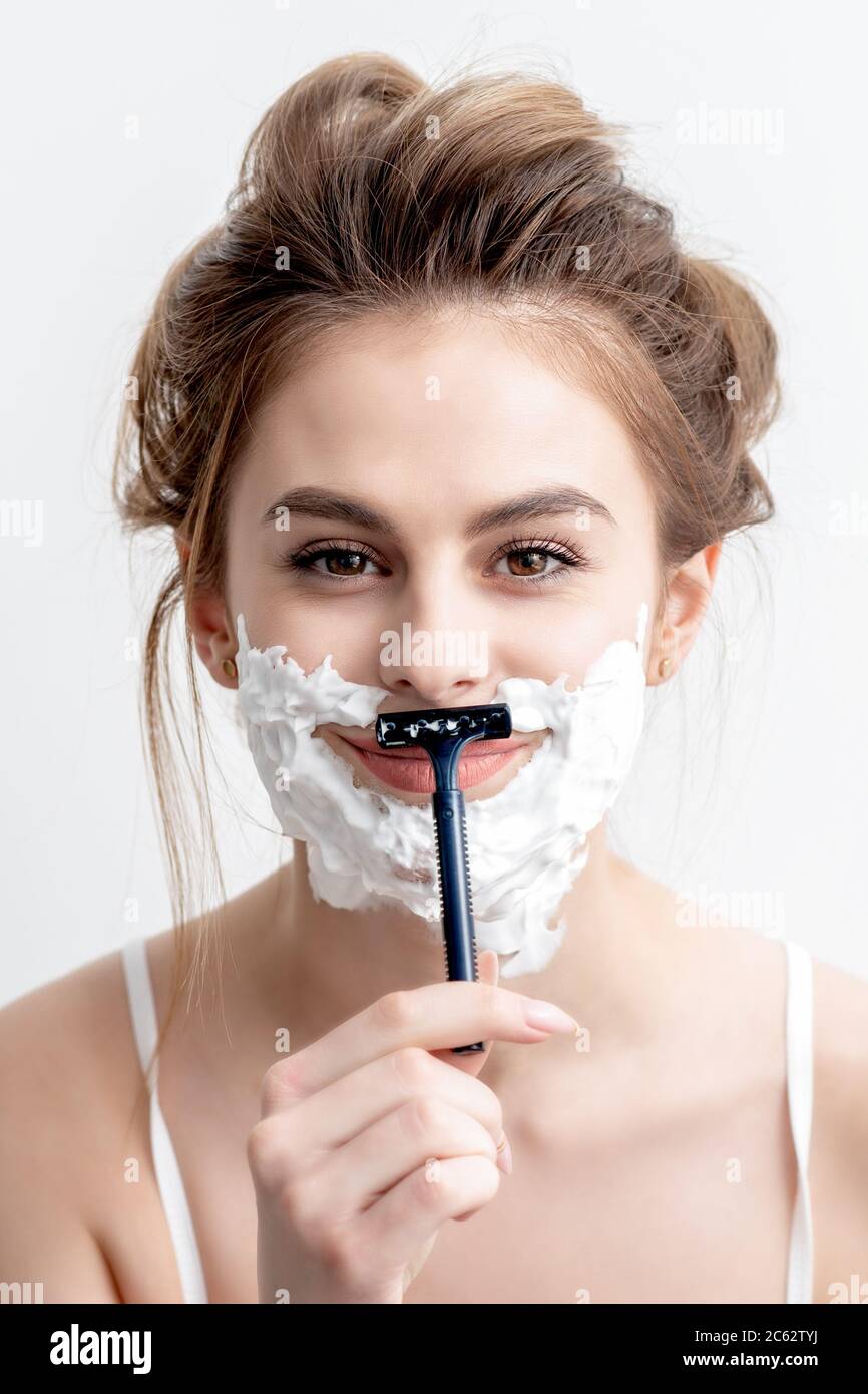 Beautiful young caucasian woman shaving her face by razor on white ...