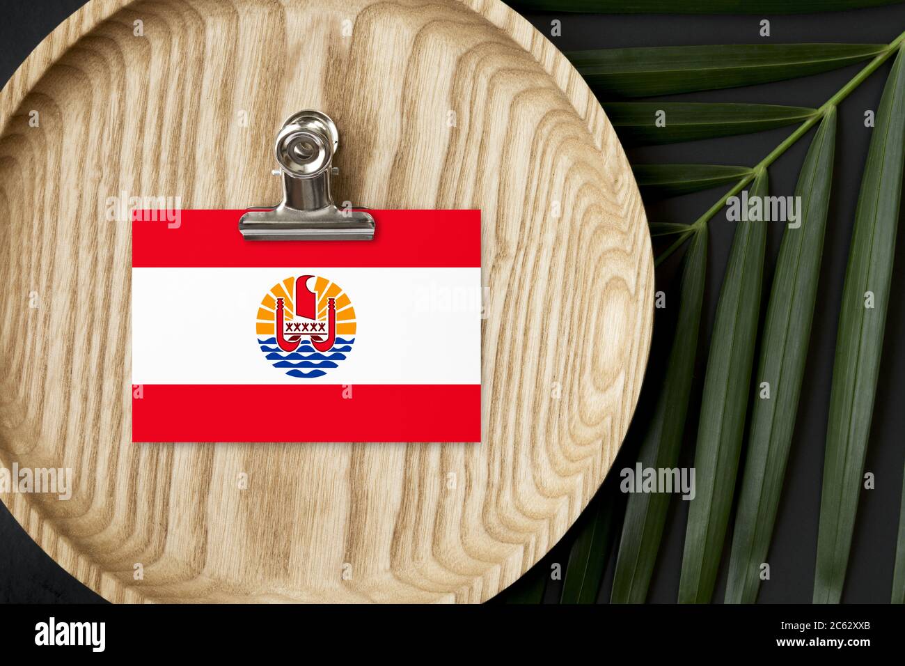 French Polynesia flag tagged on wooden plate. Tropical palm leaves ...