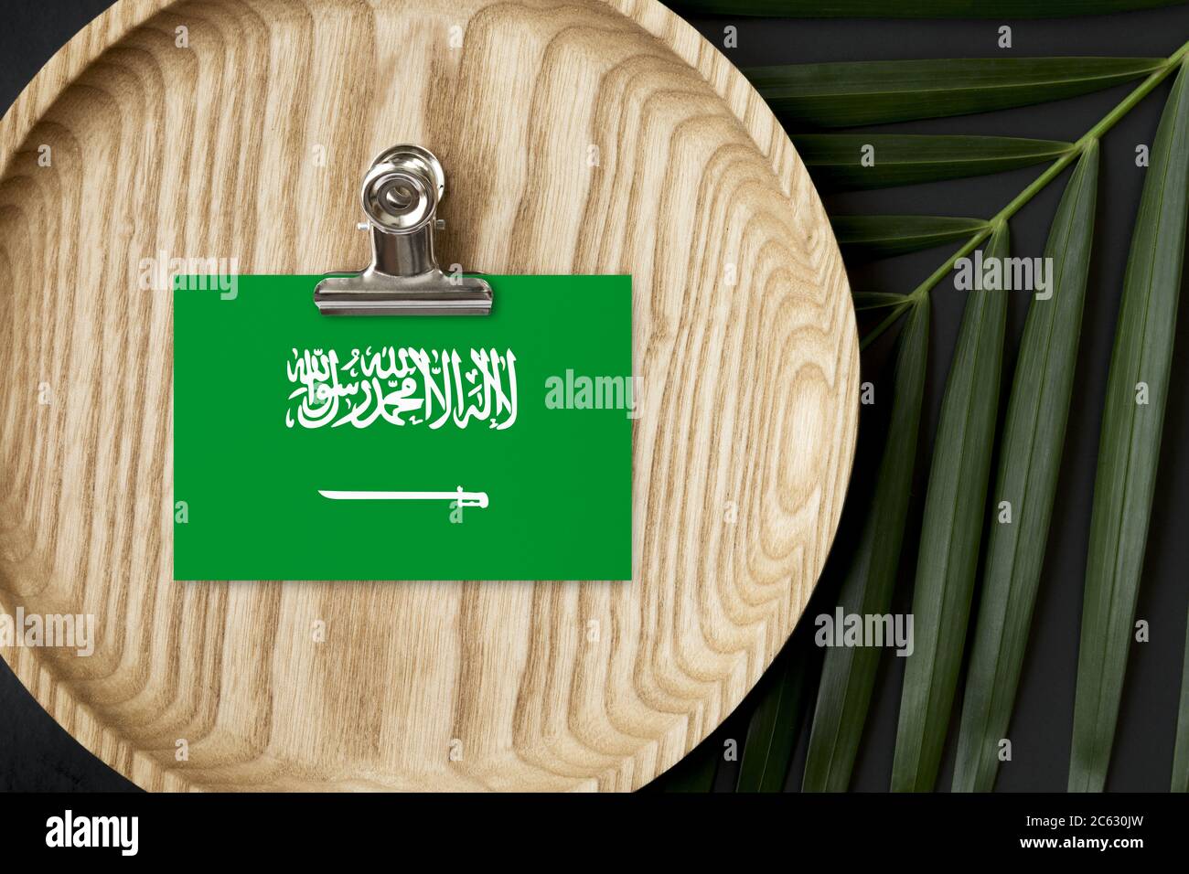 Saudi Arabia flag tagged on wooden plate. Tropical palm leaves monstera ...
