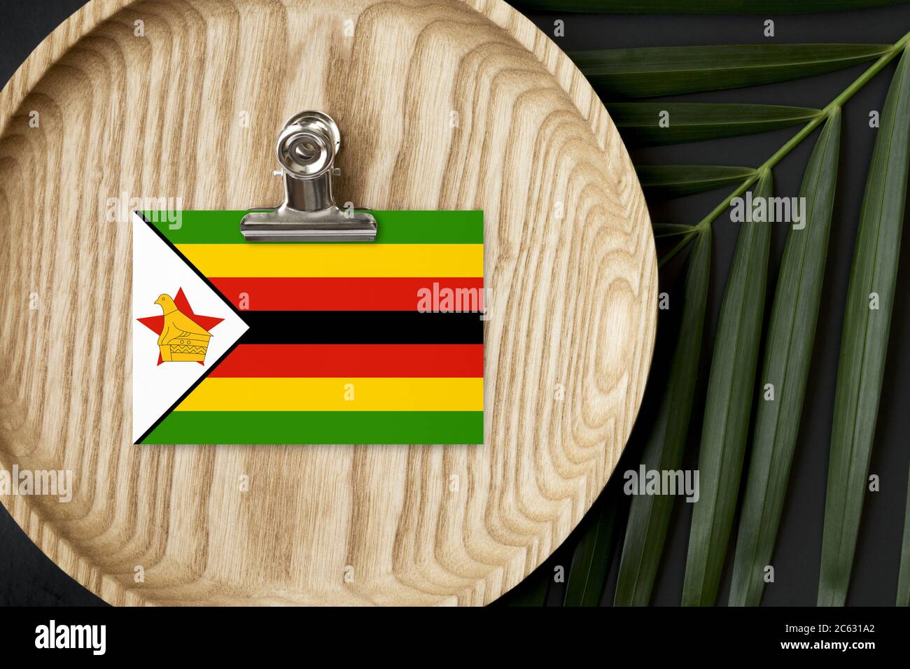 Zimbabwe flag tagged on wooden plate. Tropical palm leaves monstera on ...