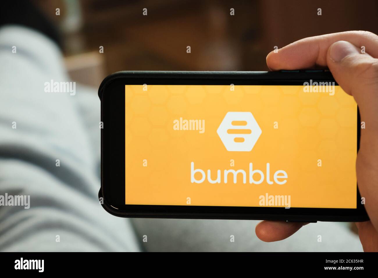 Bumble application on the smartphone in mans hand. Man laying and using ...