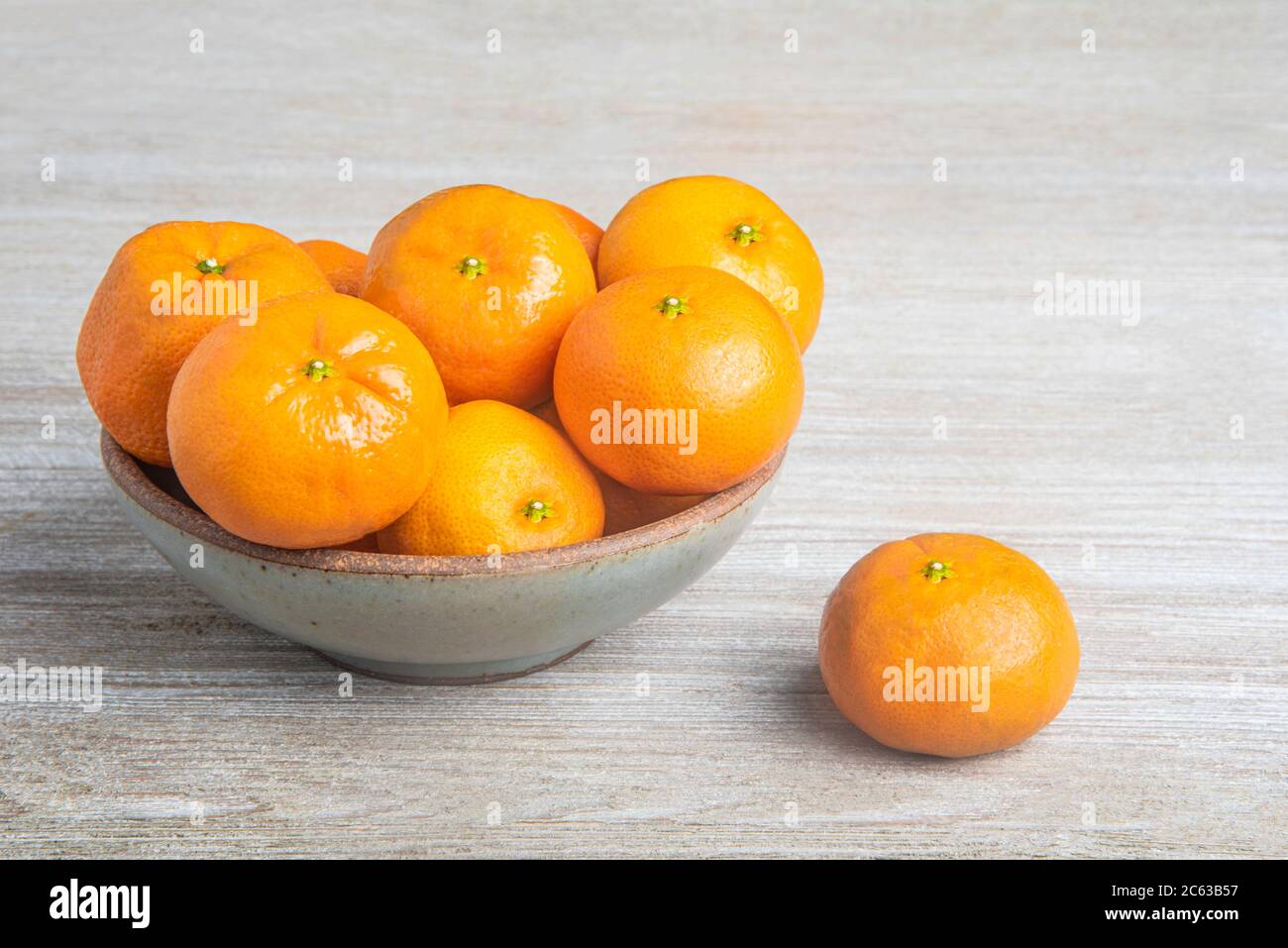 A bunch of fresh oranges in a ceramic bowl set on a white-painted ...