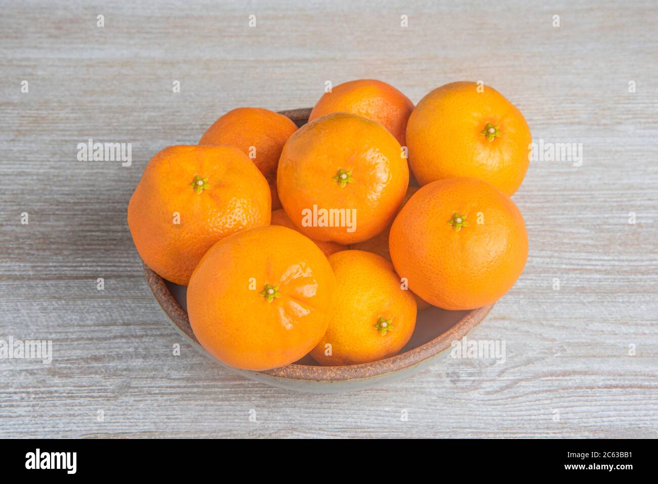 A bunch of fresh oranges in a ceramic bowl set on a white-painted ...