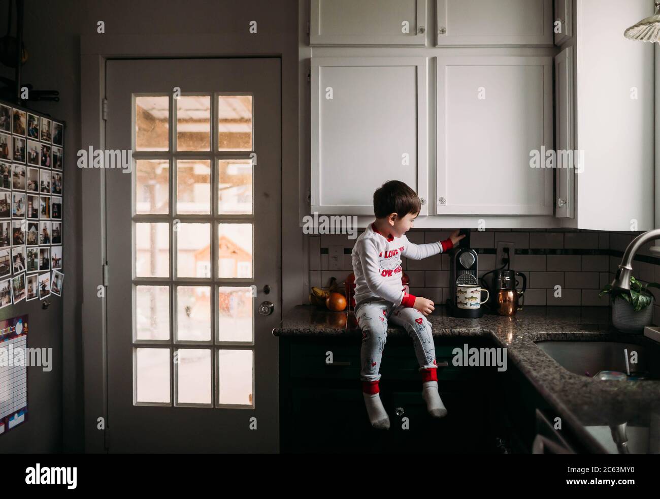Young boy sitting on kitchen counter making coffee in morning time ...