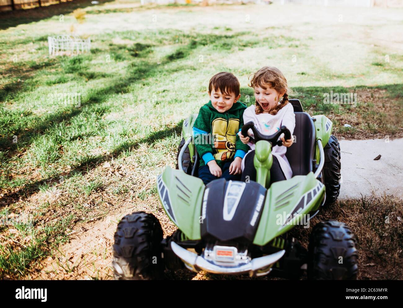 Young brother and sister riding in battery operated car and laughing ...