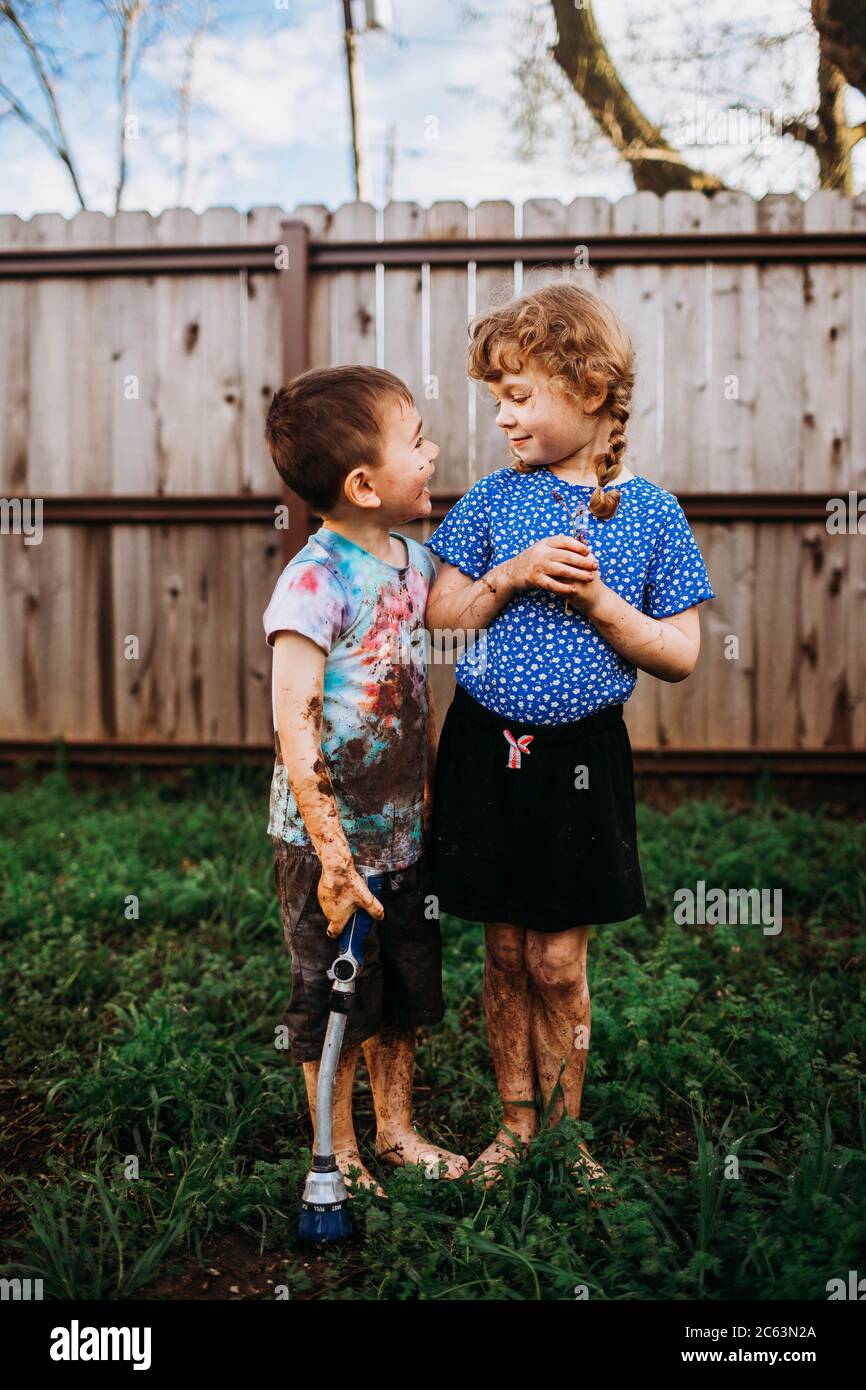 Young brother and sister covered in mud looking at each other Stock ...