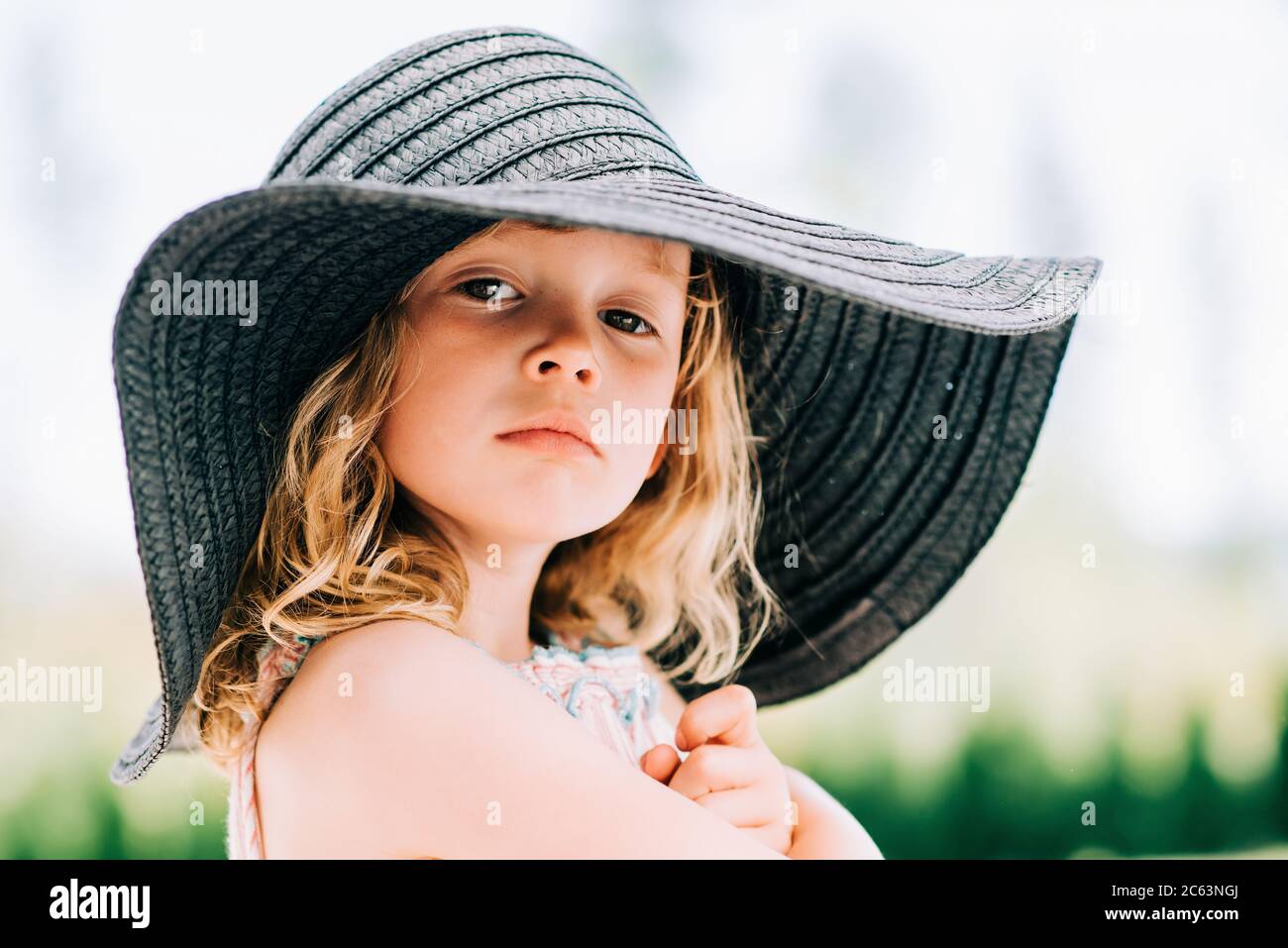 portrait of a sassy young girl staring at the camera with a sun hat on ...