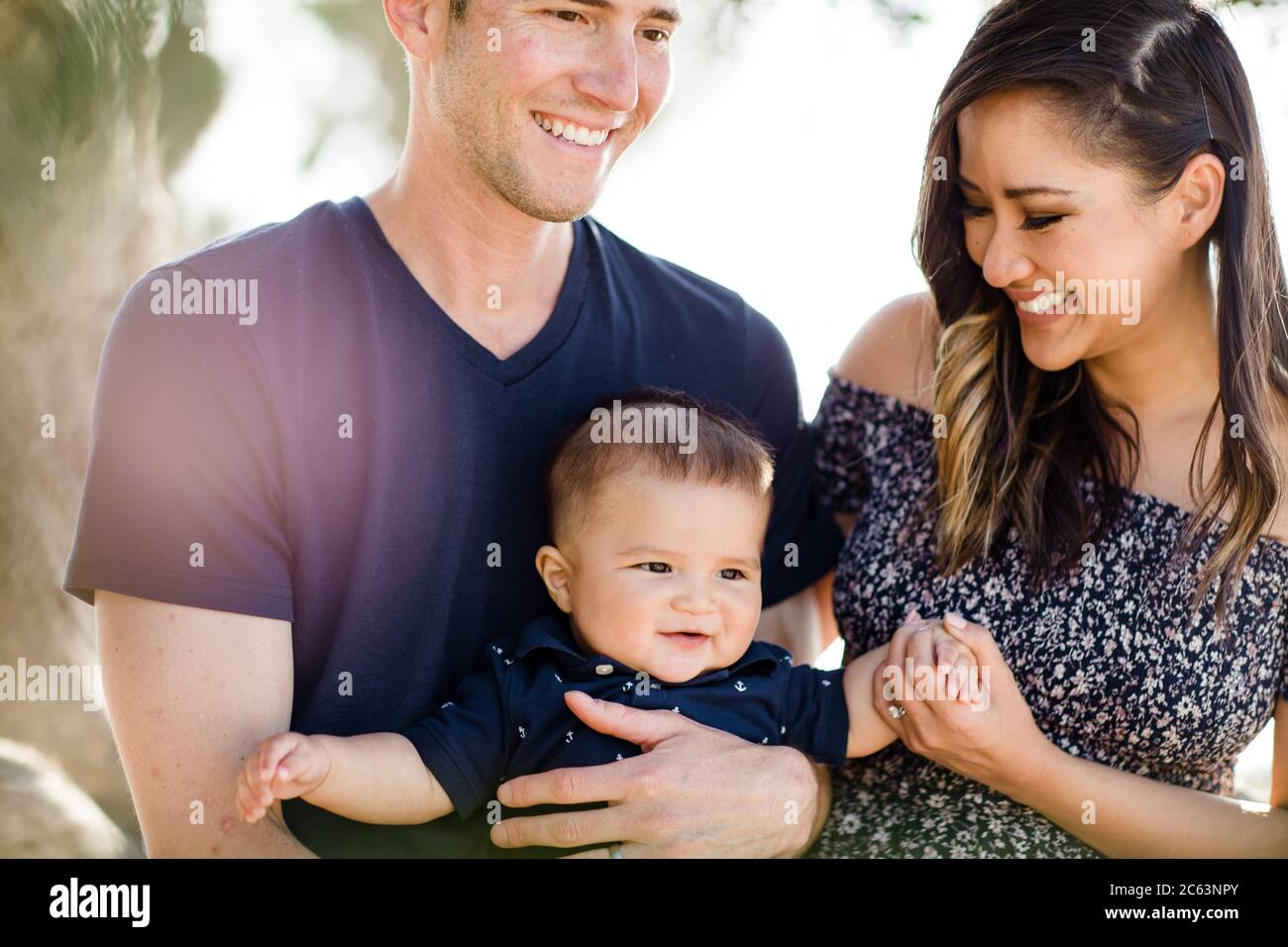 Parents Sitting Under Tree Smiling at Infant Son Stock Photo - Alamy