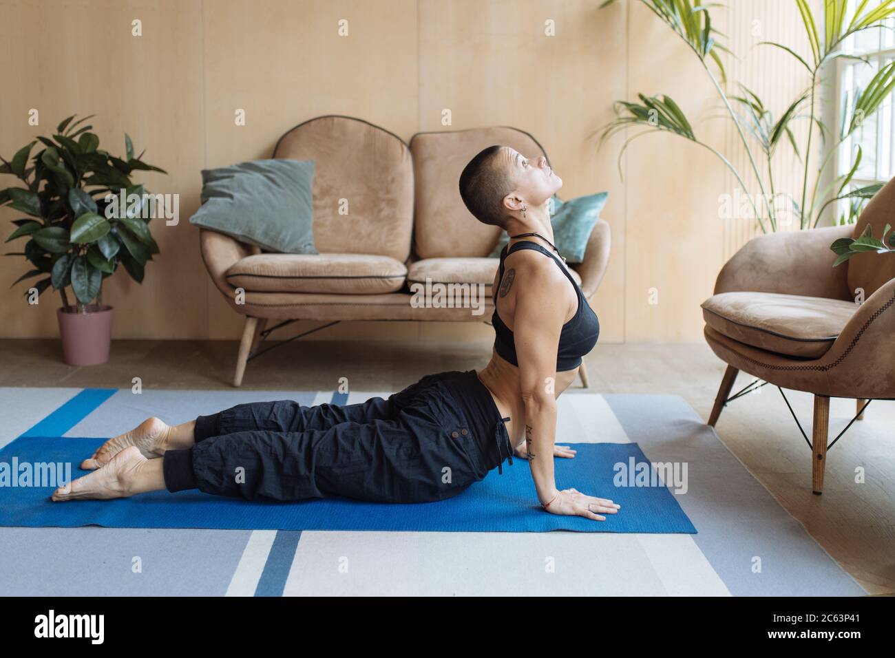 athletic skin head woman in snake yoga bhujangasana pose at home ...