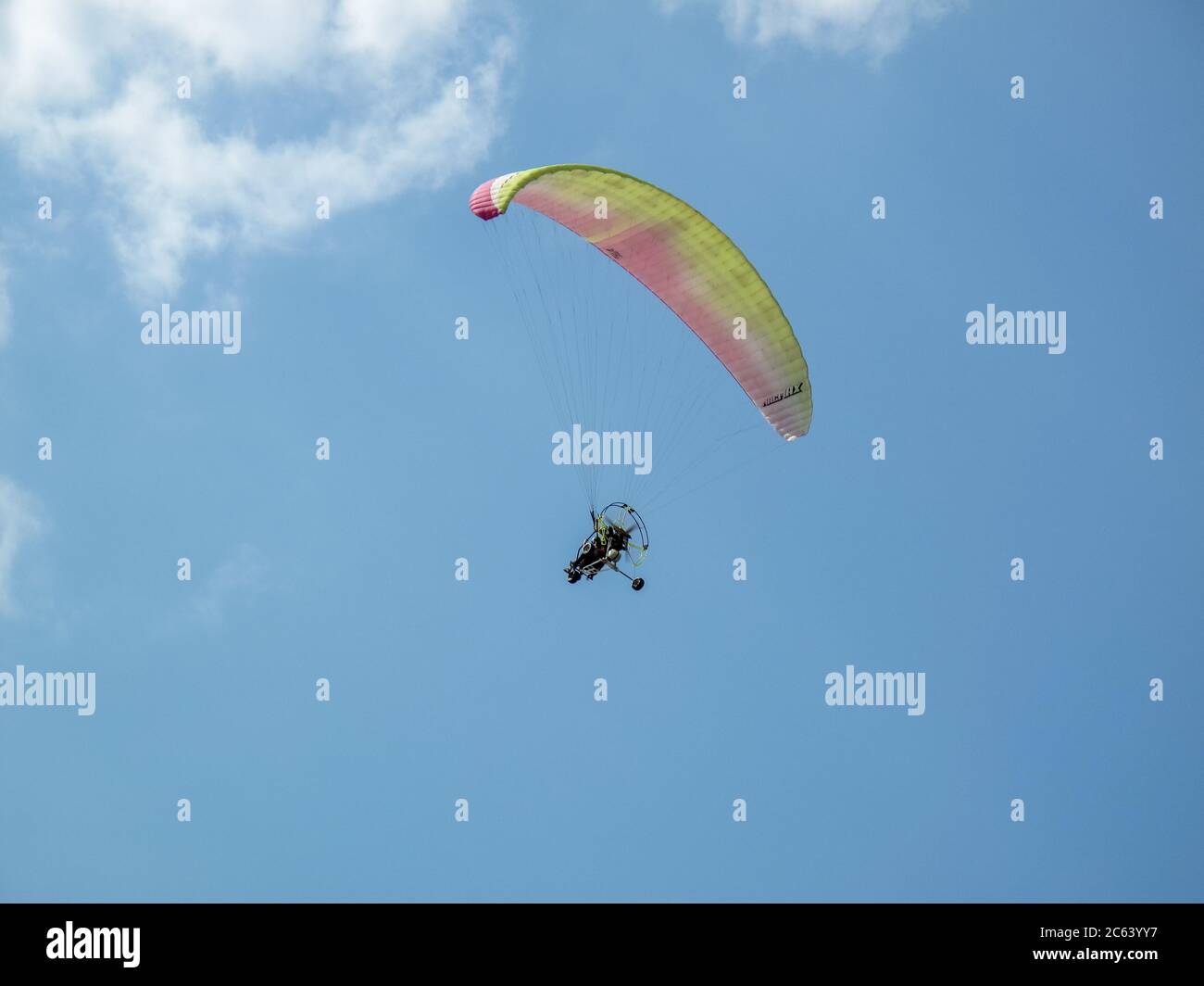 A paraglider flies in the sky under a multi-colored paraglider ...