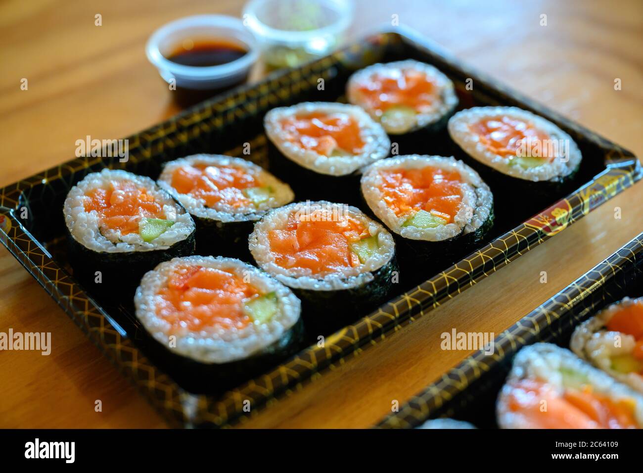 Salmon maki roll sushi on a black plastic tray, side with soy sauce and ...