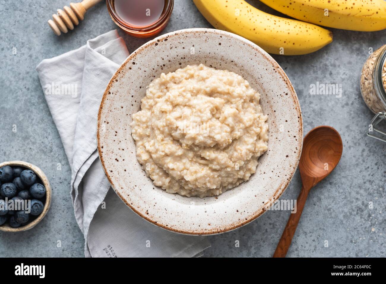Oatmeal porridge in a bowl served with bananas, blueberries and honey ...