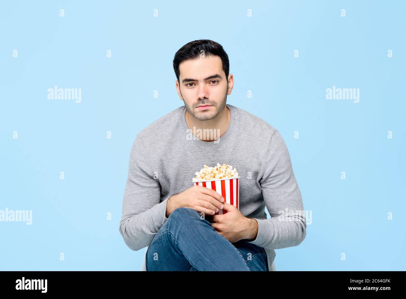 Bored young man holding popcorn sitting and watching movie isolated on ...