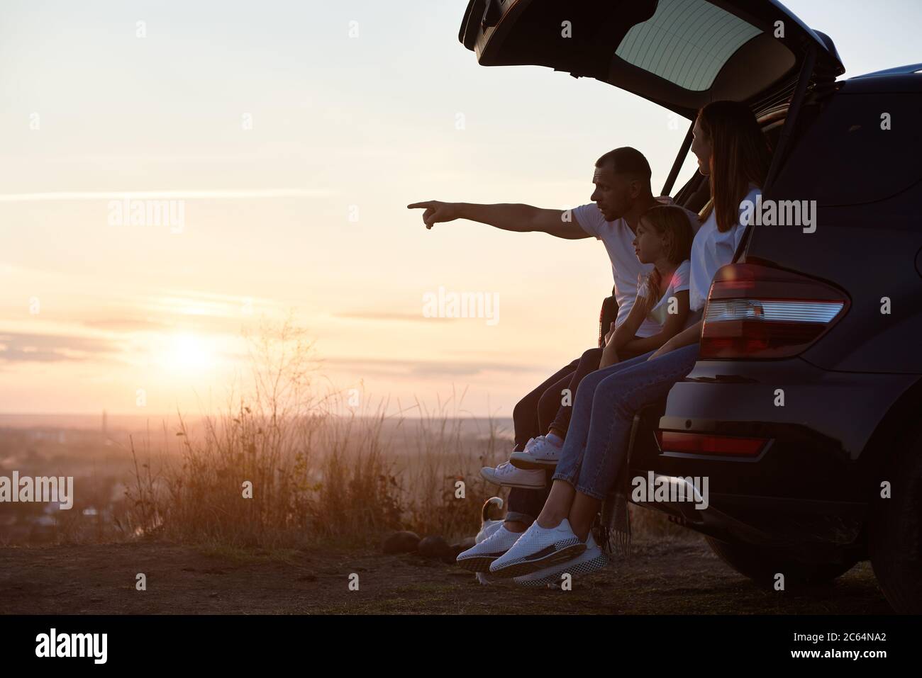 Side view of the family sitting in the car trunk outside the city on ...