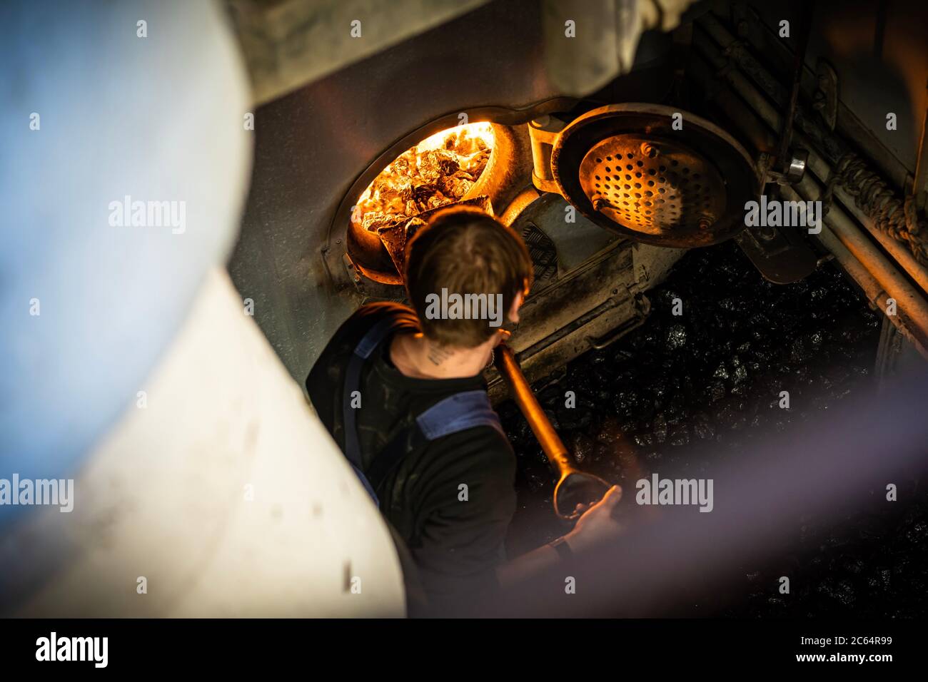 A worker insert a coal inside the engine of coaled power steam ship ...