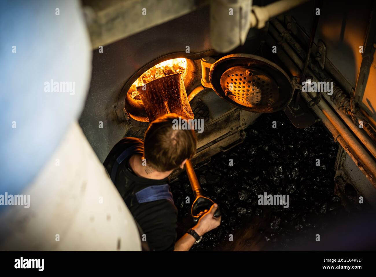 A worker insert a coal inside the engine of coaled power steam ship ...