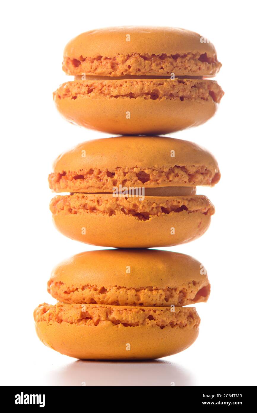 Three orange flavoured macaroons standing on top of each other on white ...