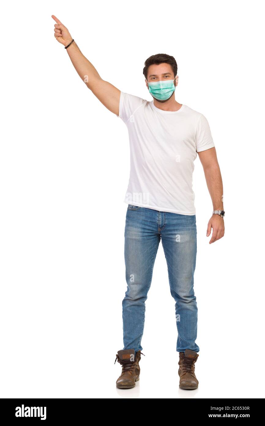 Young man in face protective mask, jeans and white t-shirt is standing ...