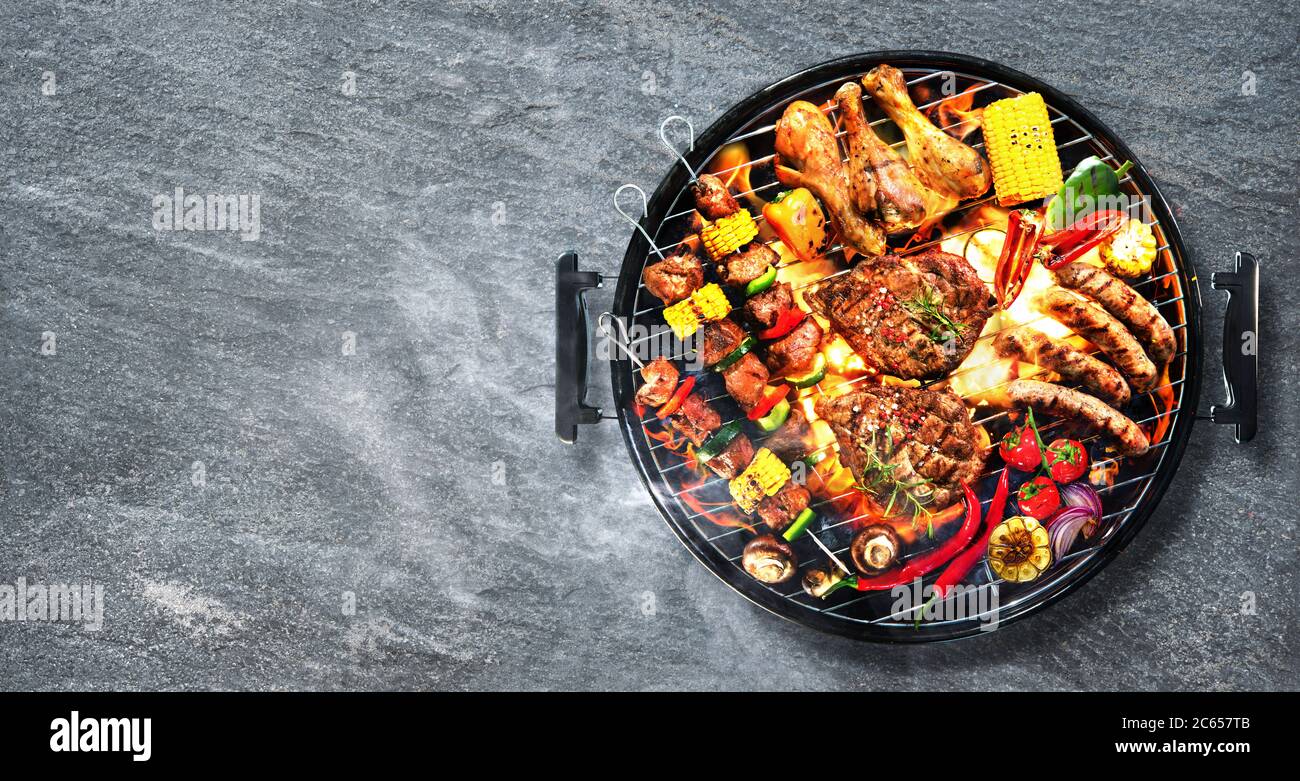 Top view of assorted delicious grilled meat with vegetables on barbecue grill with smoke and ...
