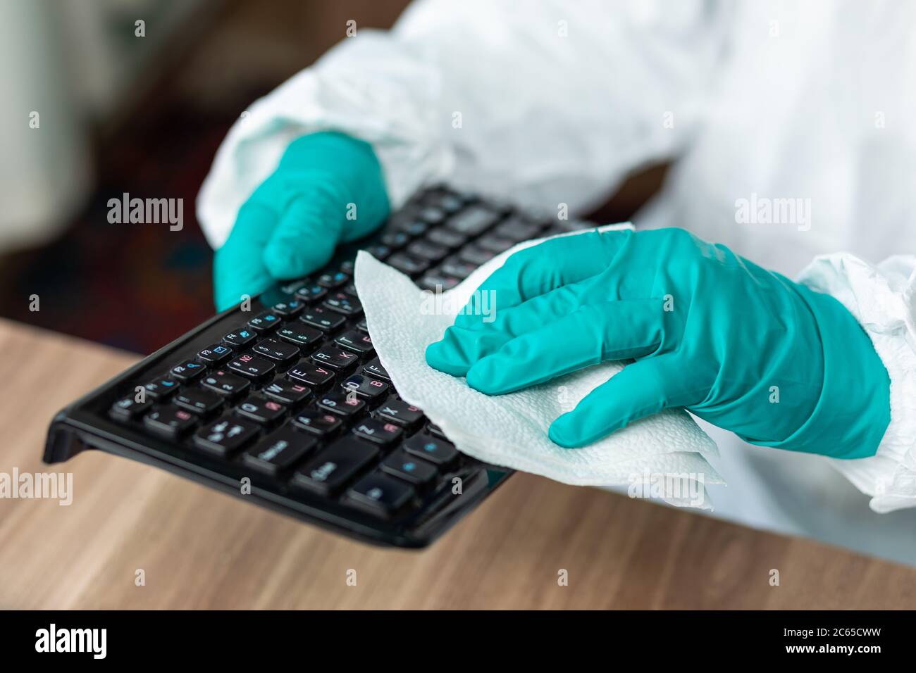 Disinfection man with special white suite cleaning a PC computer ...