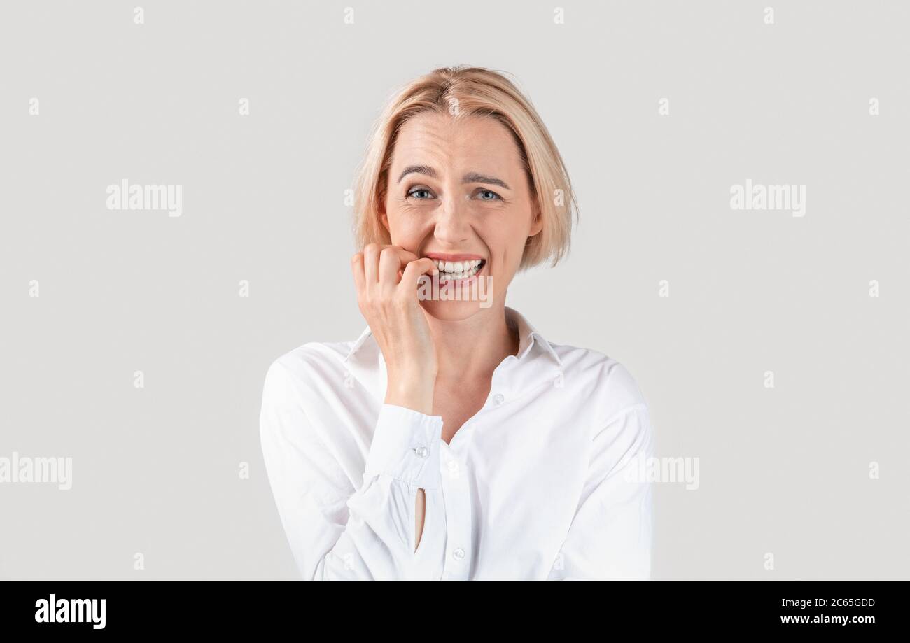 Mature secretary biting her nails in panic against light background ...