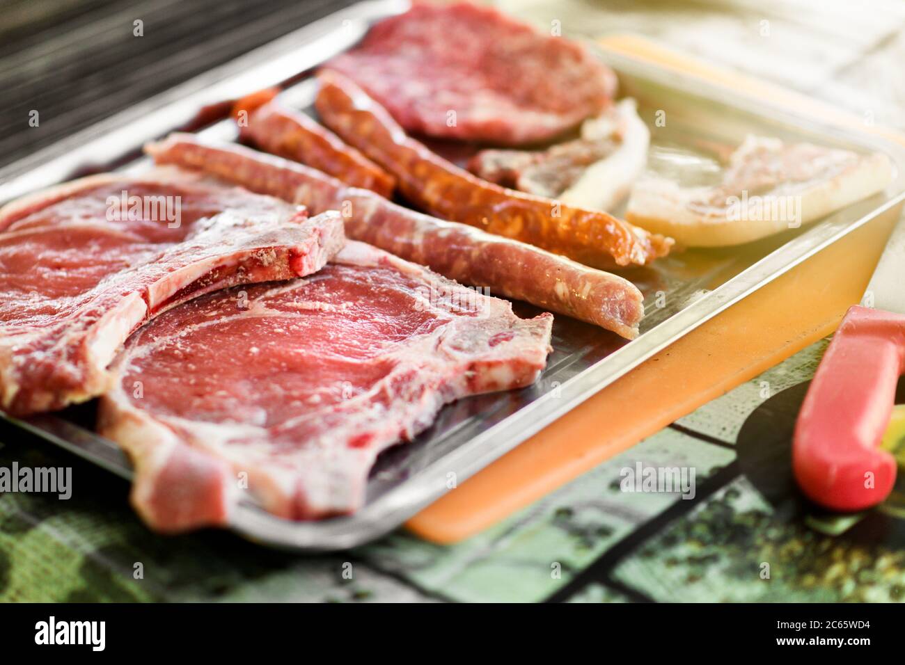 Tray with assorted raw rib eye steaks and spicy sausage ready to ...