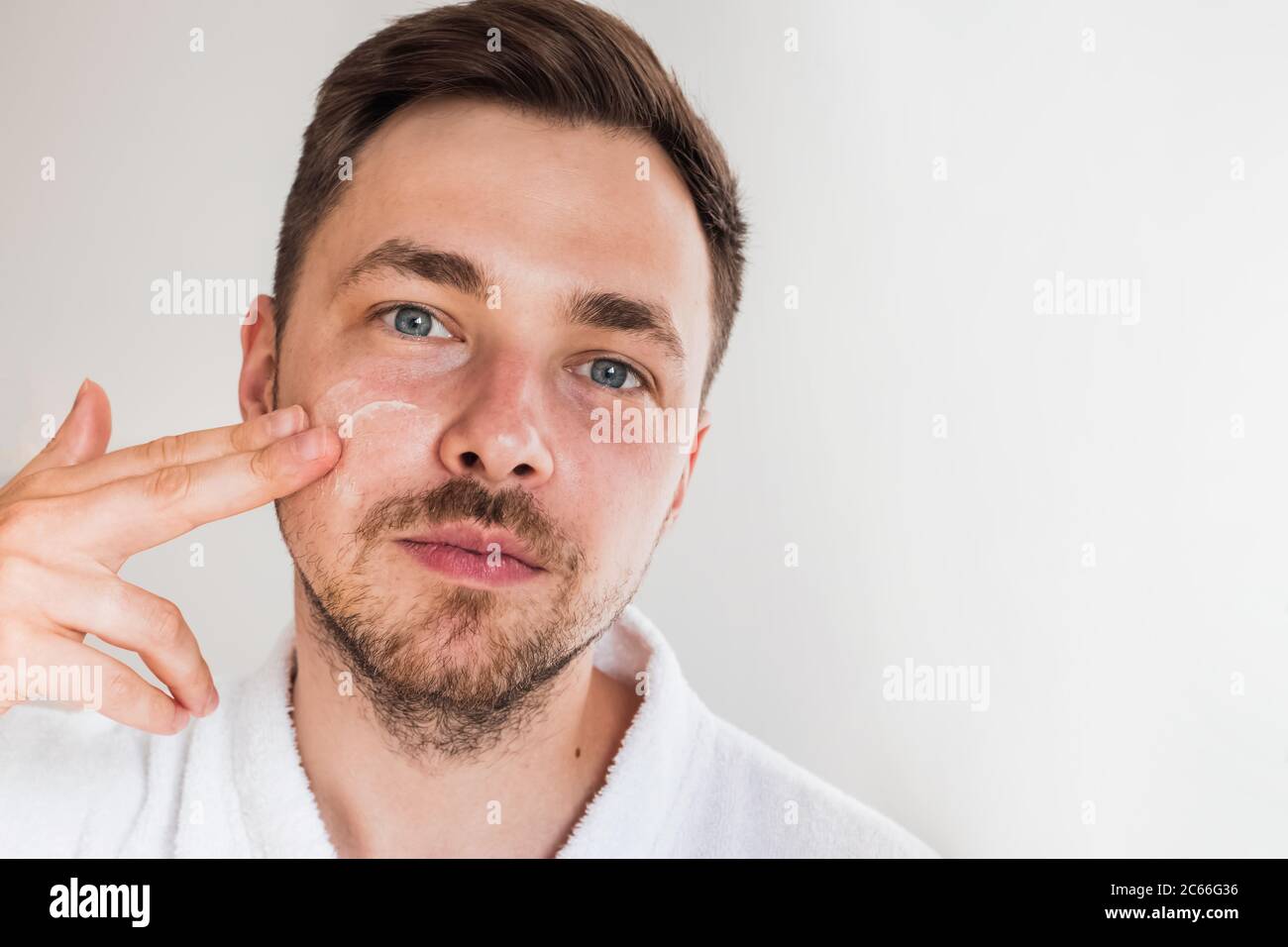 Handsome young man applying cream lotion on his face. Modern beauty and ...