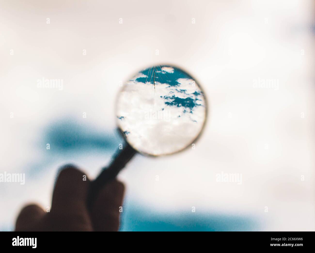 magnifying glass pointing at cloudy blue sky Stock Photo - Alamy