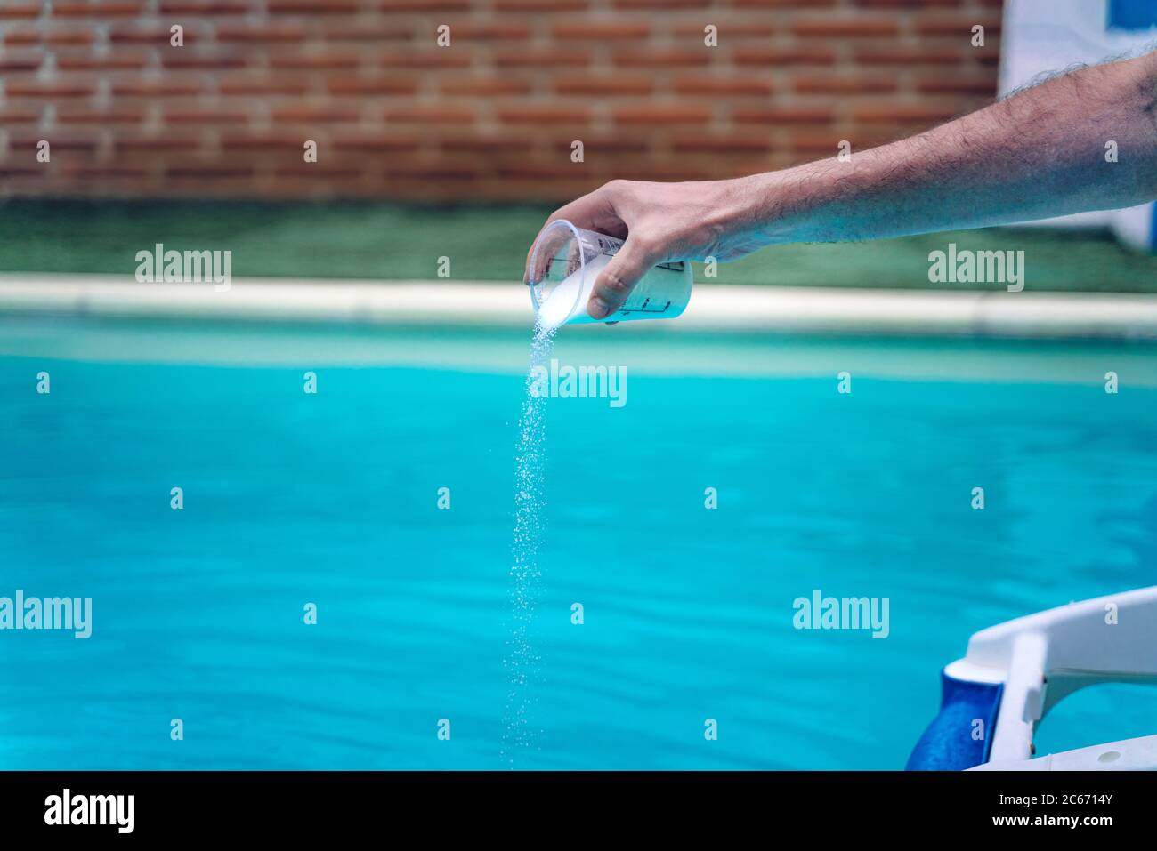 Person cleaning and chlorinating the pool on a hot summer afternoon, is ...