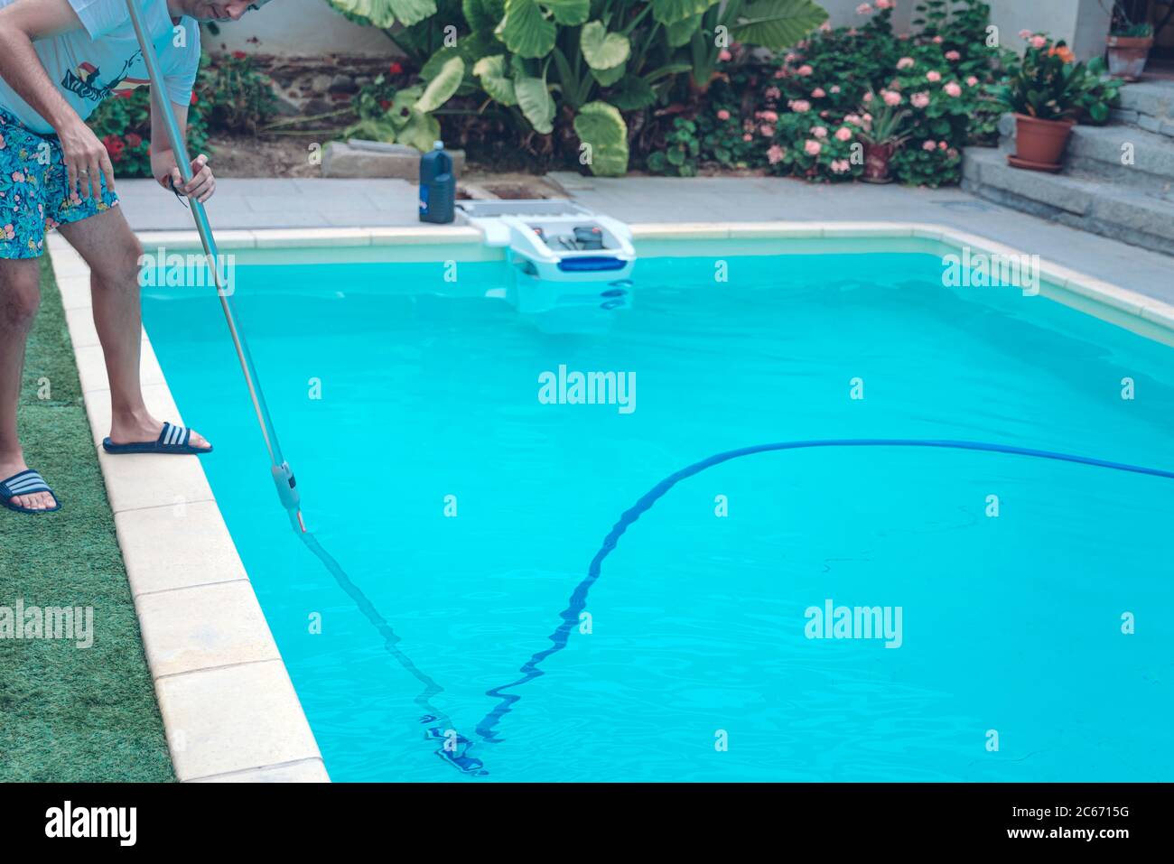 Person cleaning and chlorinating the pool on a hot summer afternoon, is ...