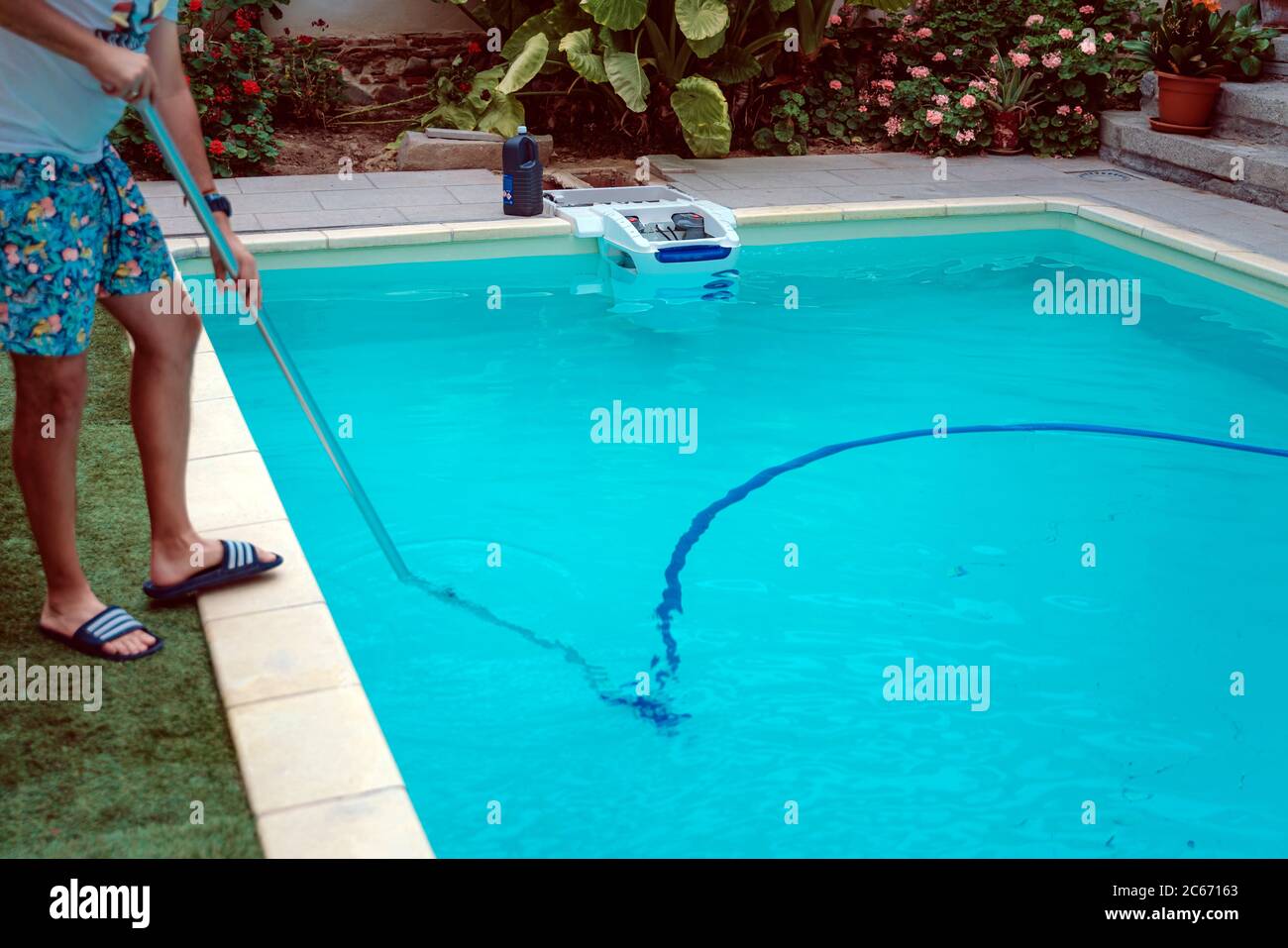 Person cleaning and chlorinating the pool on a hot summer afternoon, is ...