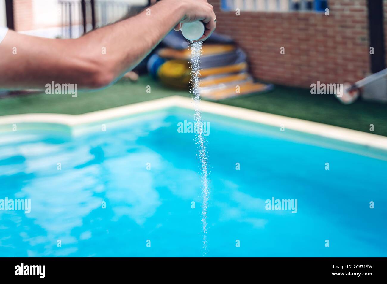 Person cleaning and chlorinating the pool on a hot summer afternoon, is ...