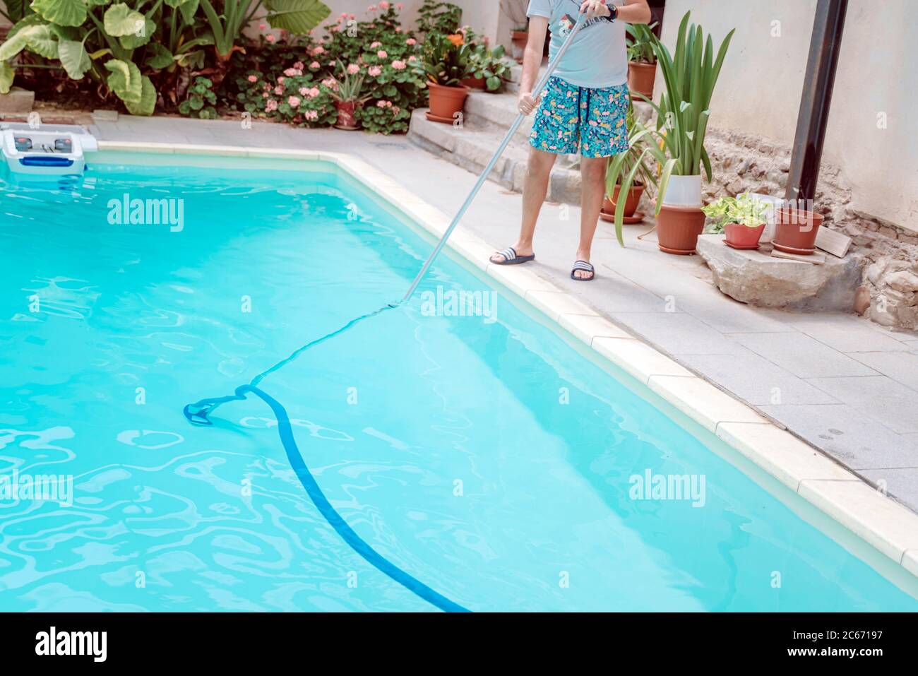 Person cleaning and chlorinating the pool on a hot summer afternoon, is ...
