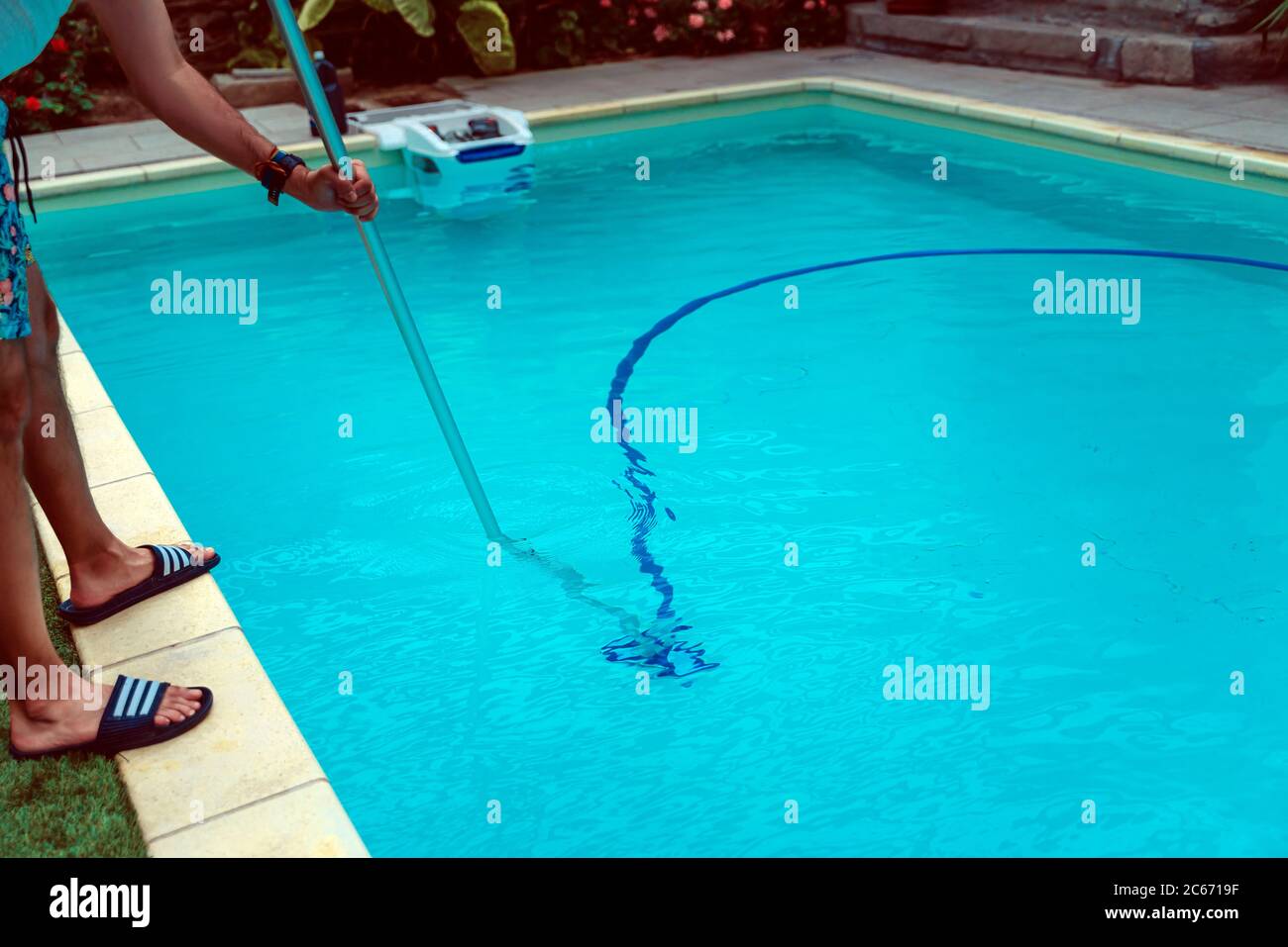 Person cleaning and chlorinating the pool on a hot summer afternoon, is ...