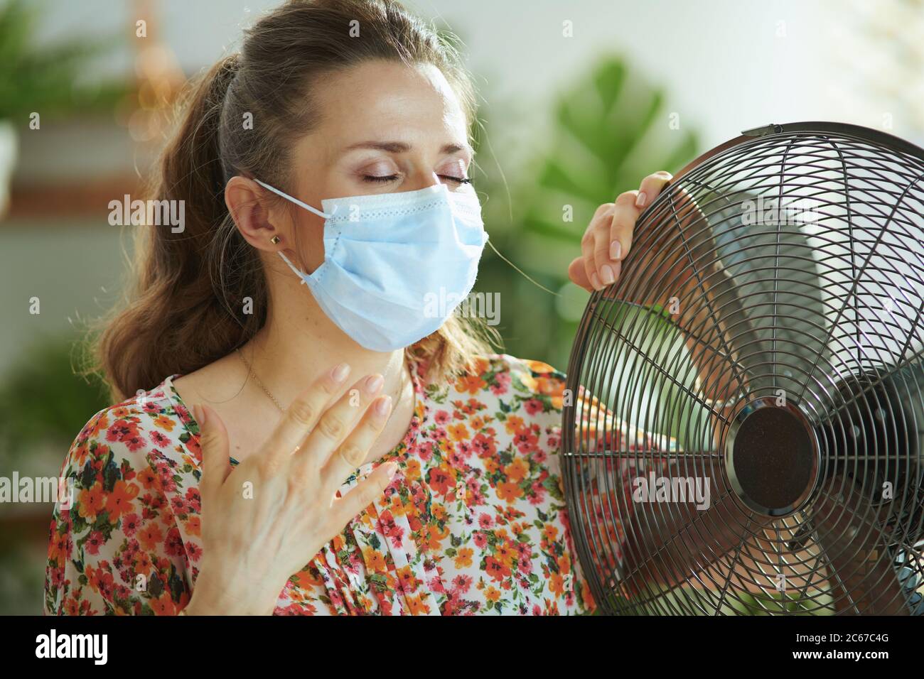 Summer heat. sad middle aged woman in floral blouse with electric fan ...