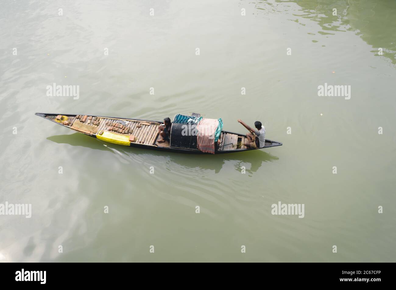 A fisherman rowing his narrow fishing boat in the Ganges river ...