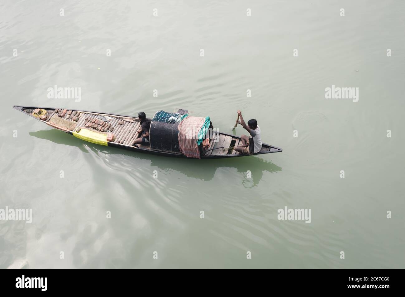 A fisherman rowing his narrow fishing boat in the Ganges river ...