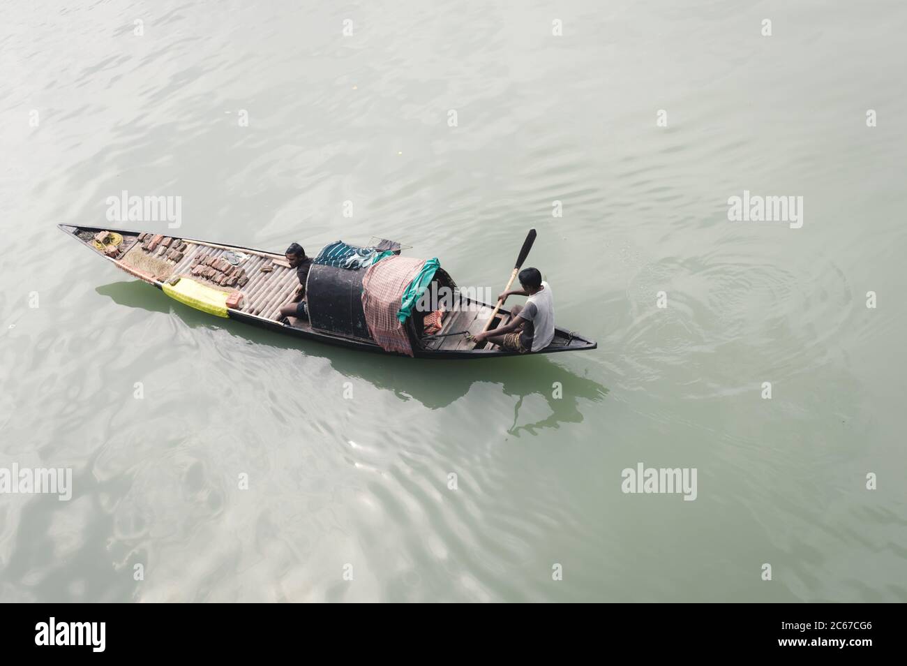 A fisherman rowing his narrow fishing boat in the Ganges river ...