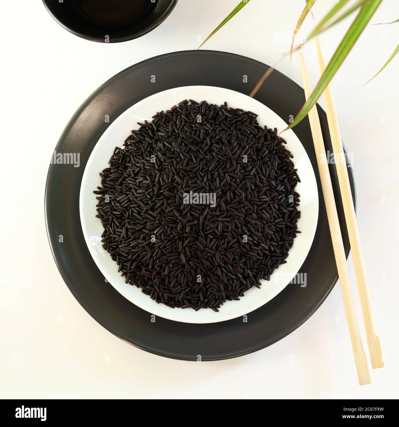 Black rice in a plate with wooden chopsticks on white background ...