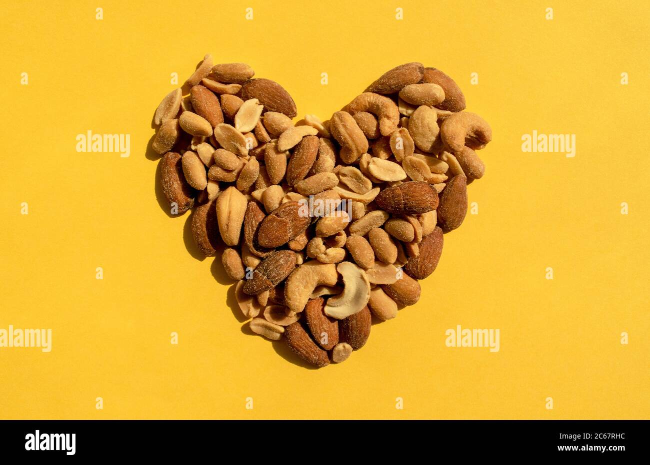Various nuts in a heart shape on yellow background. Top view. Different ...