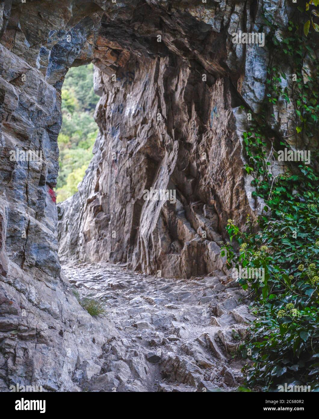 A hole in the mountain side as a rocky pathway winds alongside the ...