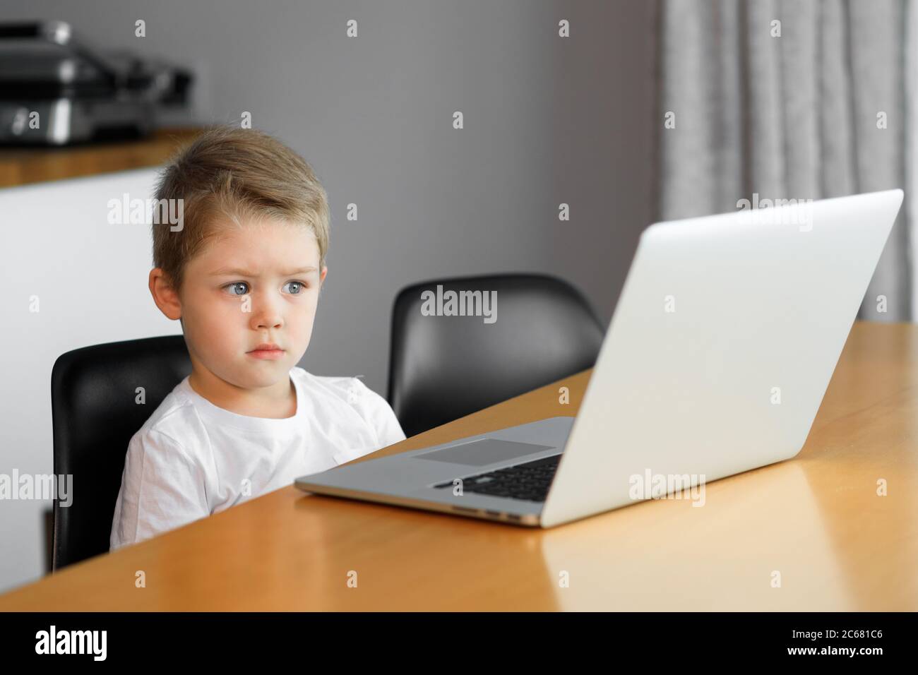 A young boy using a laptop computer sitting on top of a table at home ...
