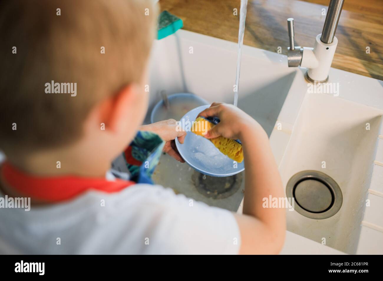 a boy in an apron washes dishes in the kitchen at home Stock Photo - Alamy