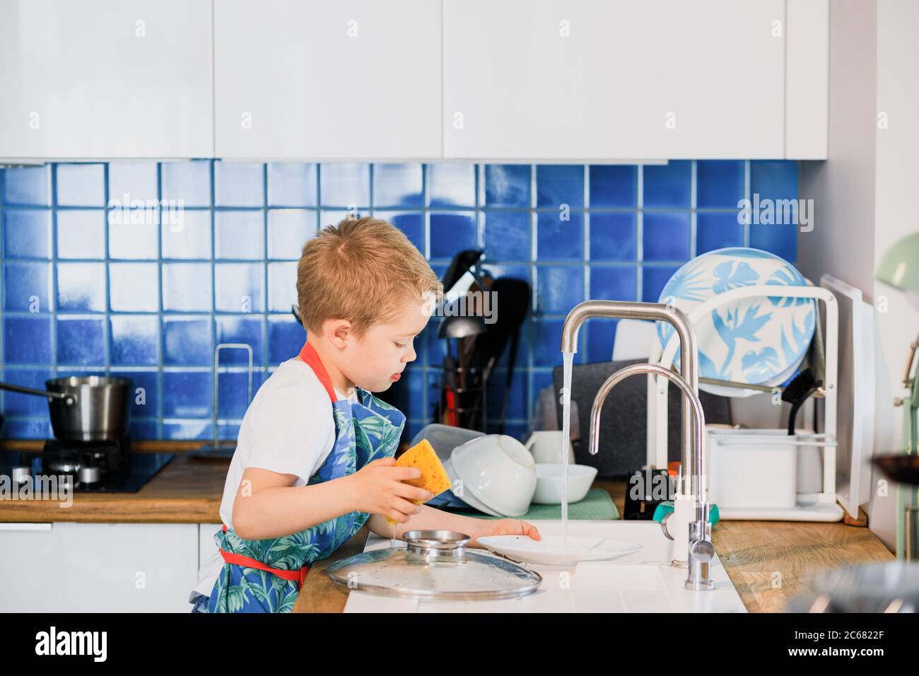 a boy in an apron washes dishes in the kitchen at home Stock Photo - Alamy