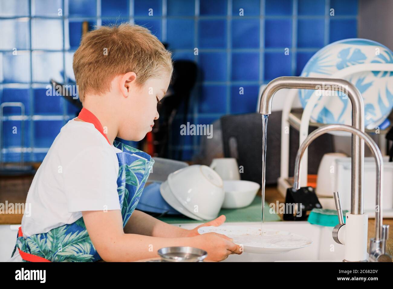 a boy in an apron washes dishes in the kitchen at home Stock Photo - Alamy