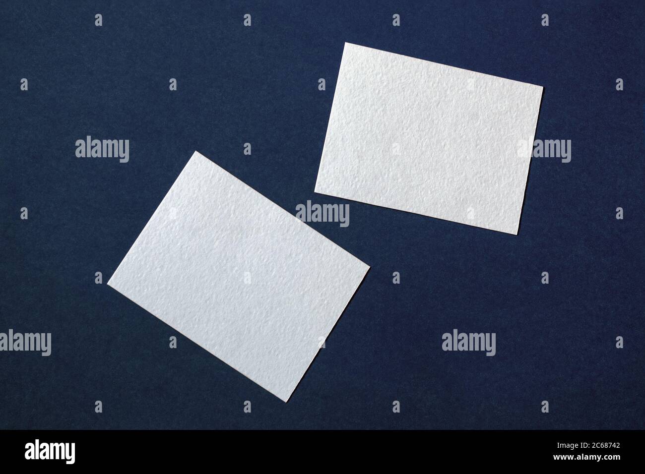two white paper cards on dark blue textured background, randomly placed ...