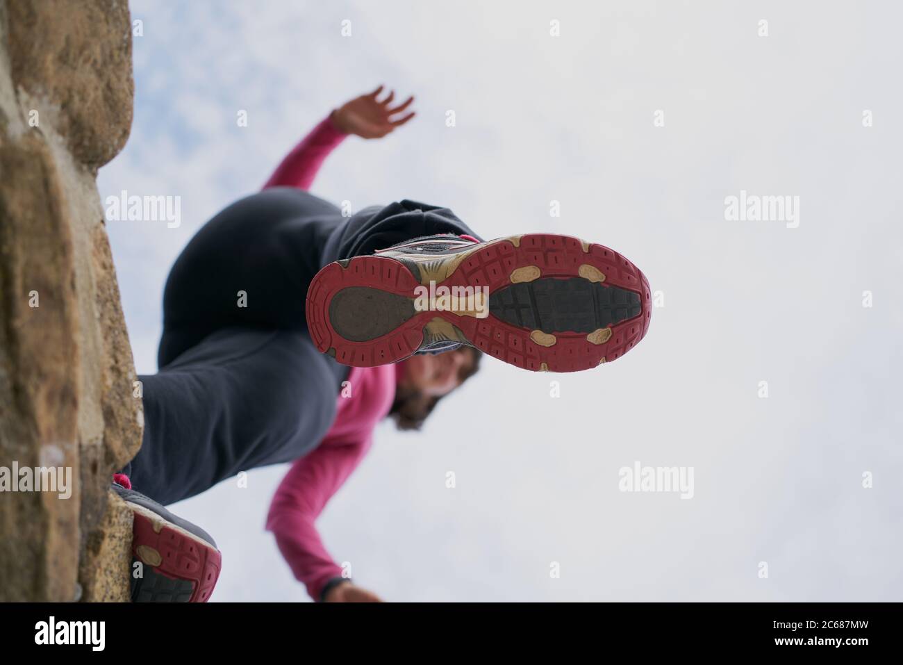 From below female in sneakers jumping from rough stone wall against ...