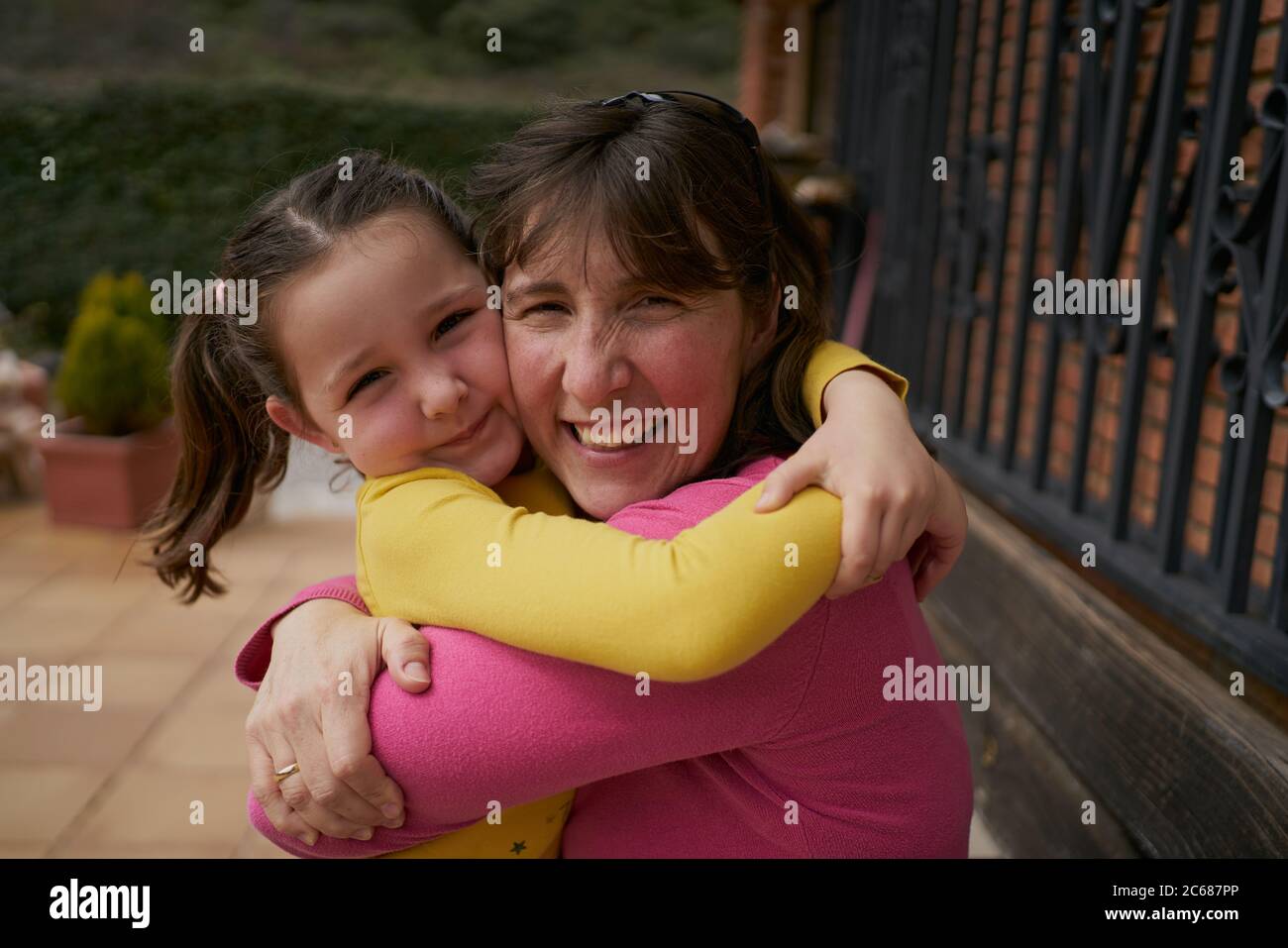 Side view of cheerful woman hugging daughter while resting on bench in ...