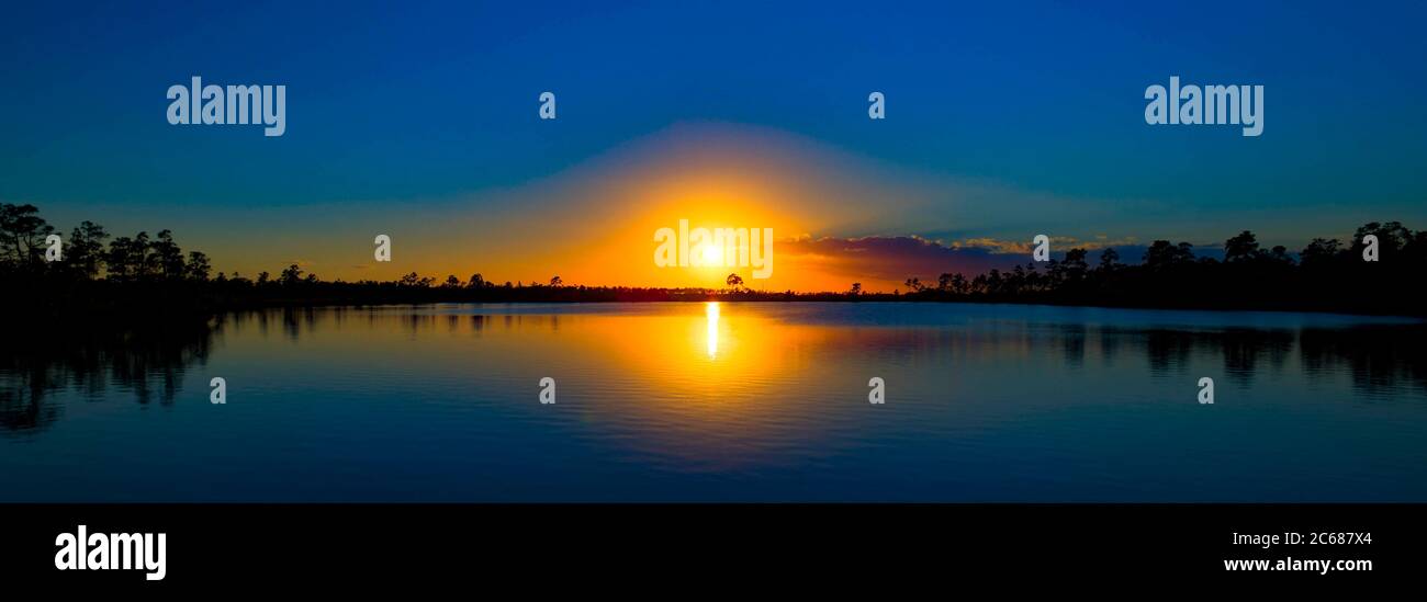 View of lake reflecting sun and forest at sunset in Everglades National ...