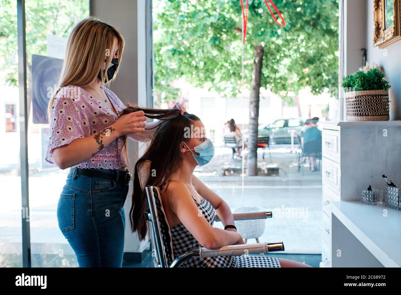 a hairdresser wearking a face mask making curls at the beatuy saloon ...